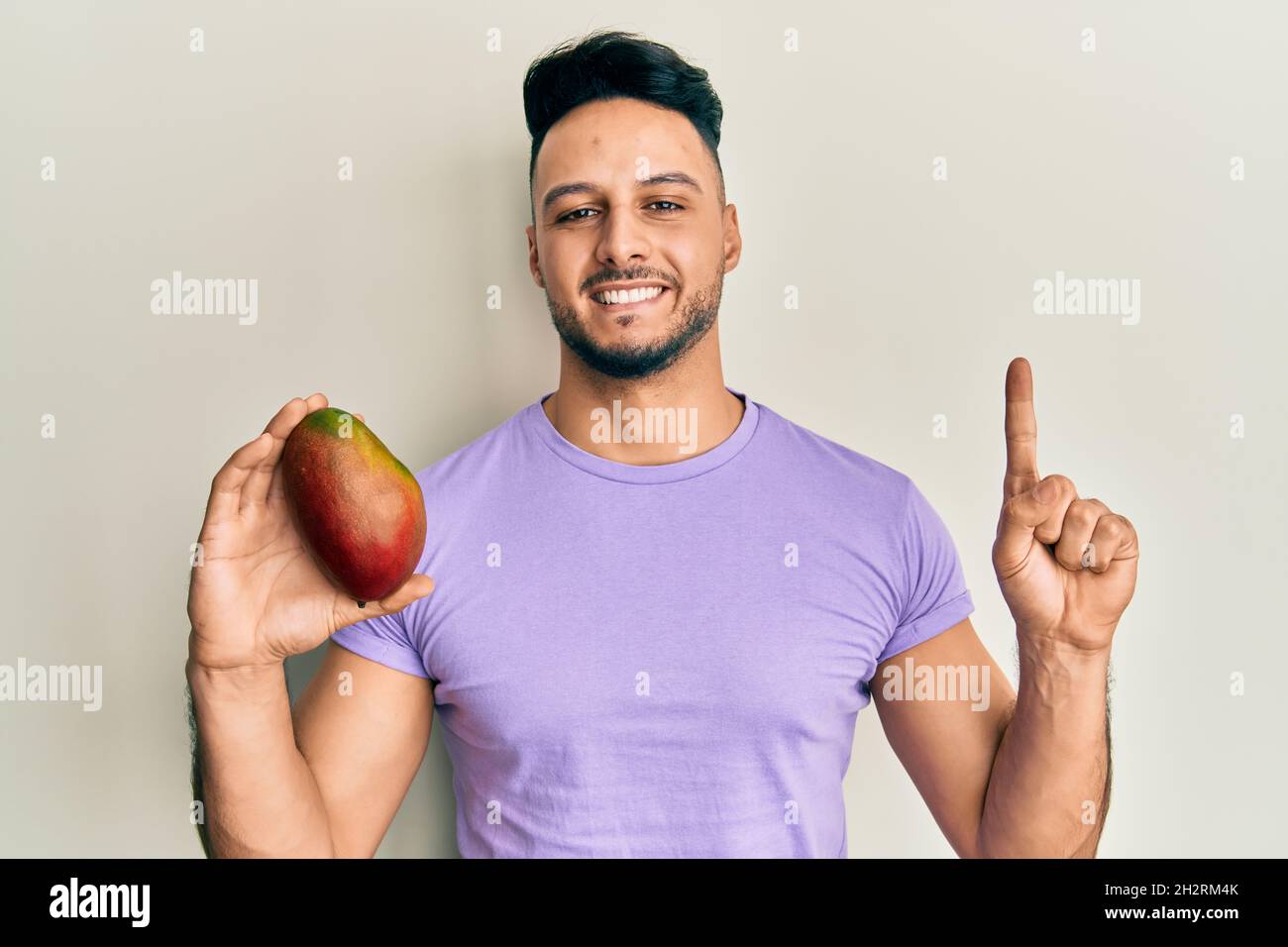 Young arab man holding mango smiling with an idea or question pointing ...