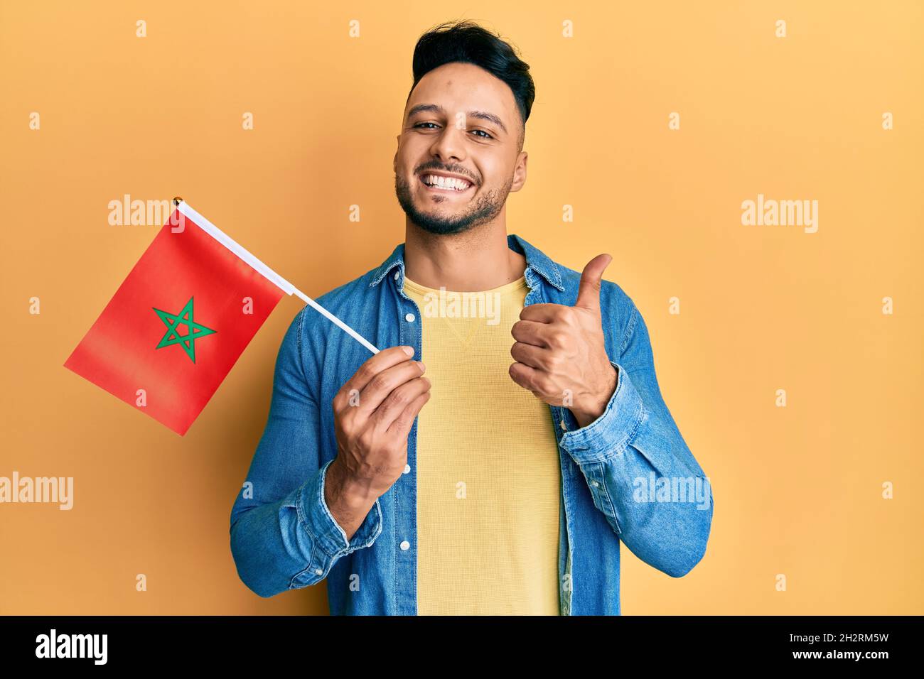 Young arab man holding morocco flag smiling happy and positive, thumb ...