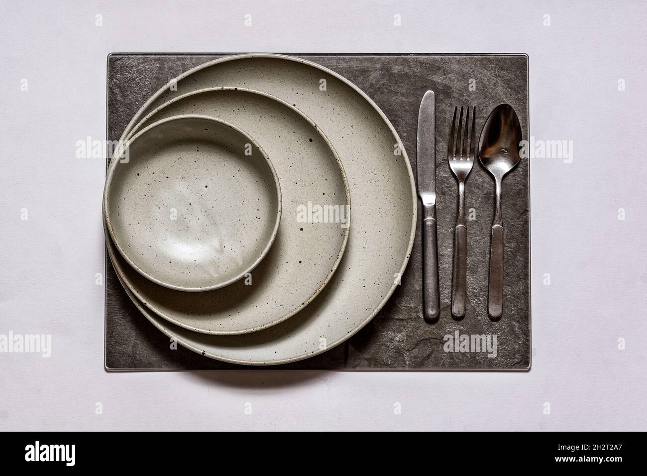 A top view of layers of dining plates with spoon, fork, and knife on a ...