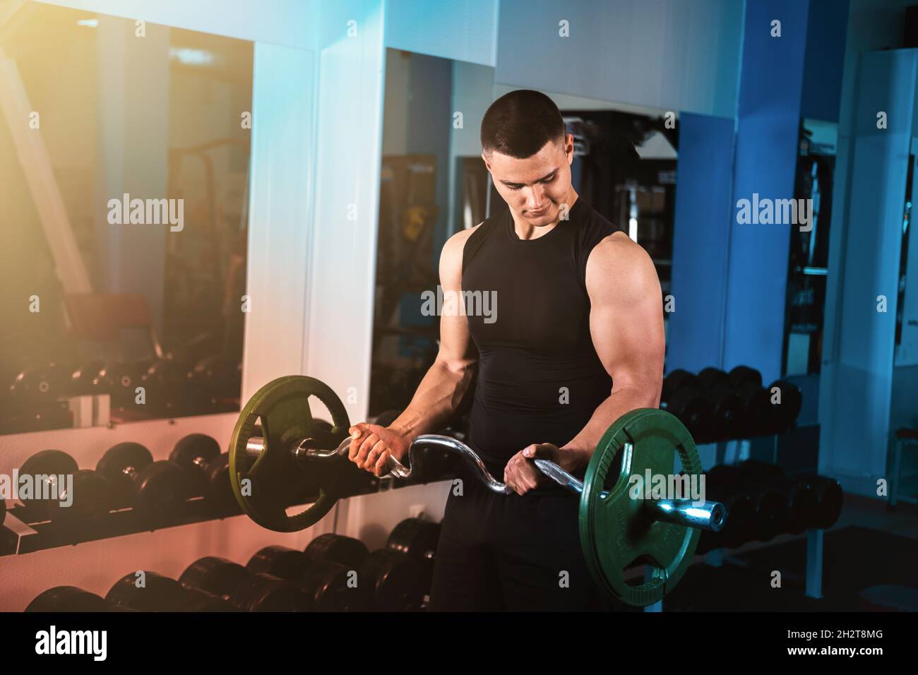 A young athlete does exercises for biceps, a barbell with a curved bar ...