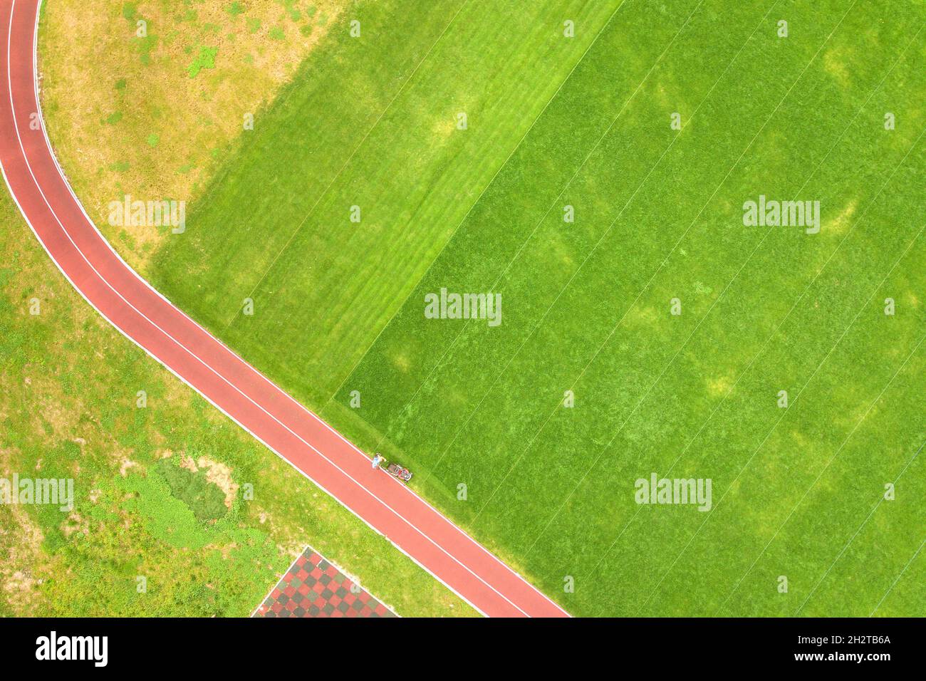 Aerial view of small figure of worker cutting green grass with mowing ...