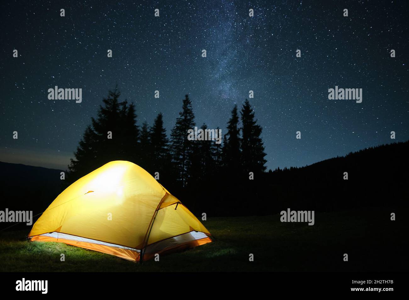 Brightly illuminated camping tent glowing on campsite in dark mountains ...