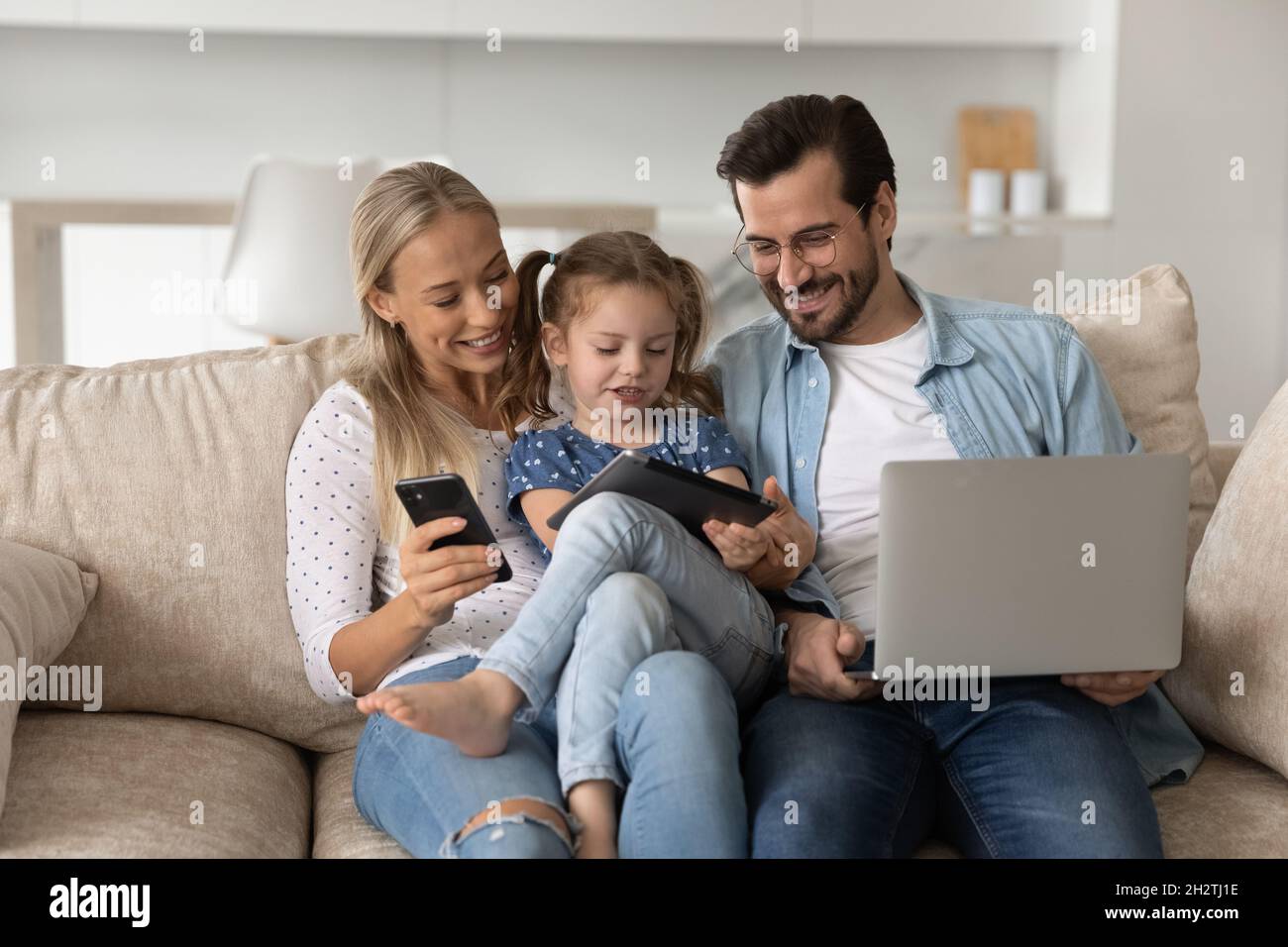 Happy bonding family couple and little kid using different gadgets ...