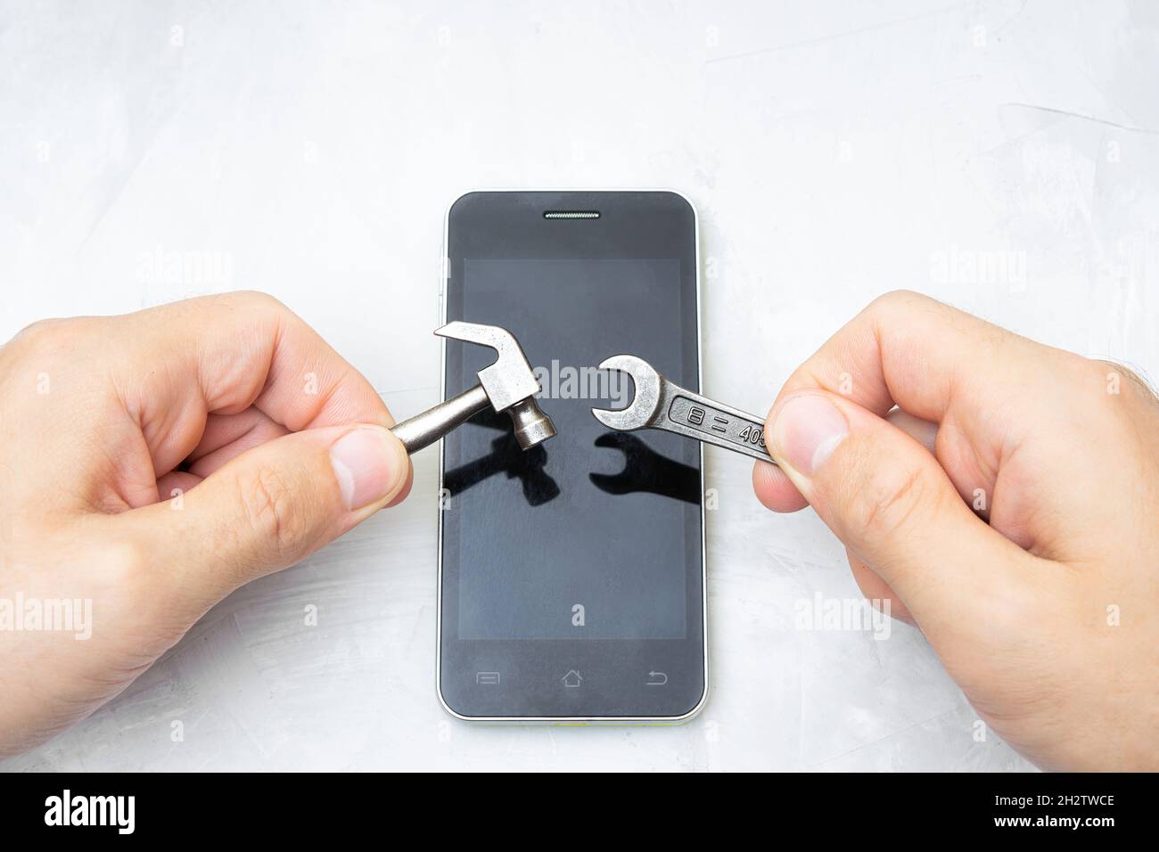 Hands holding small hand tools over a smartphone on a concrete table ...
