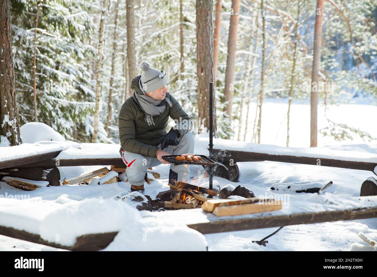Man roasting sausages on campfire in forest by the lake, making a fire ...