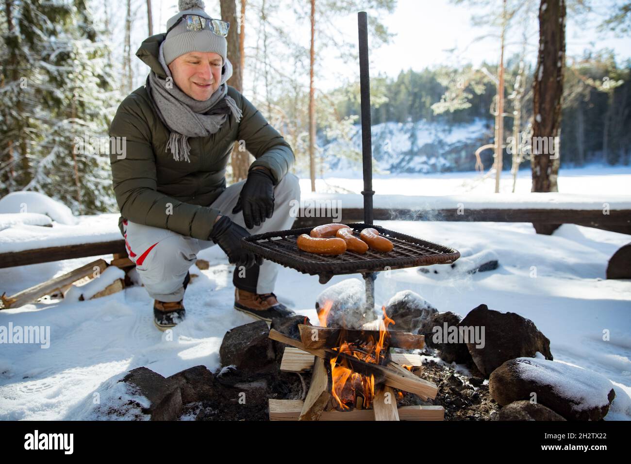 Man roasting sausages on campfire in forest by the lake, making a fire ...