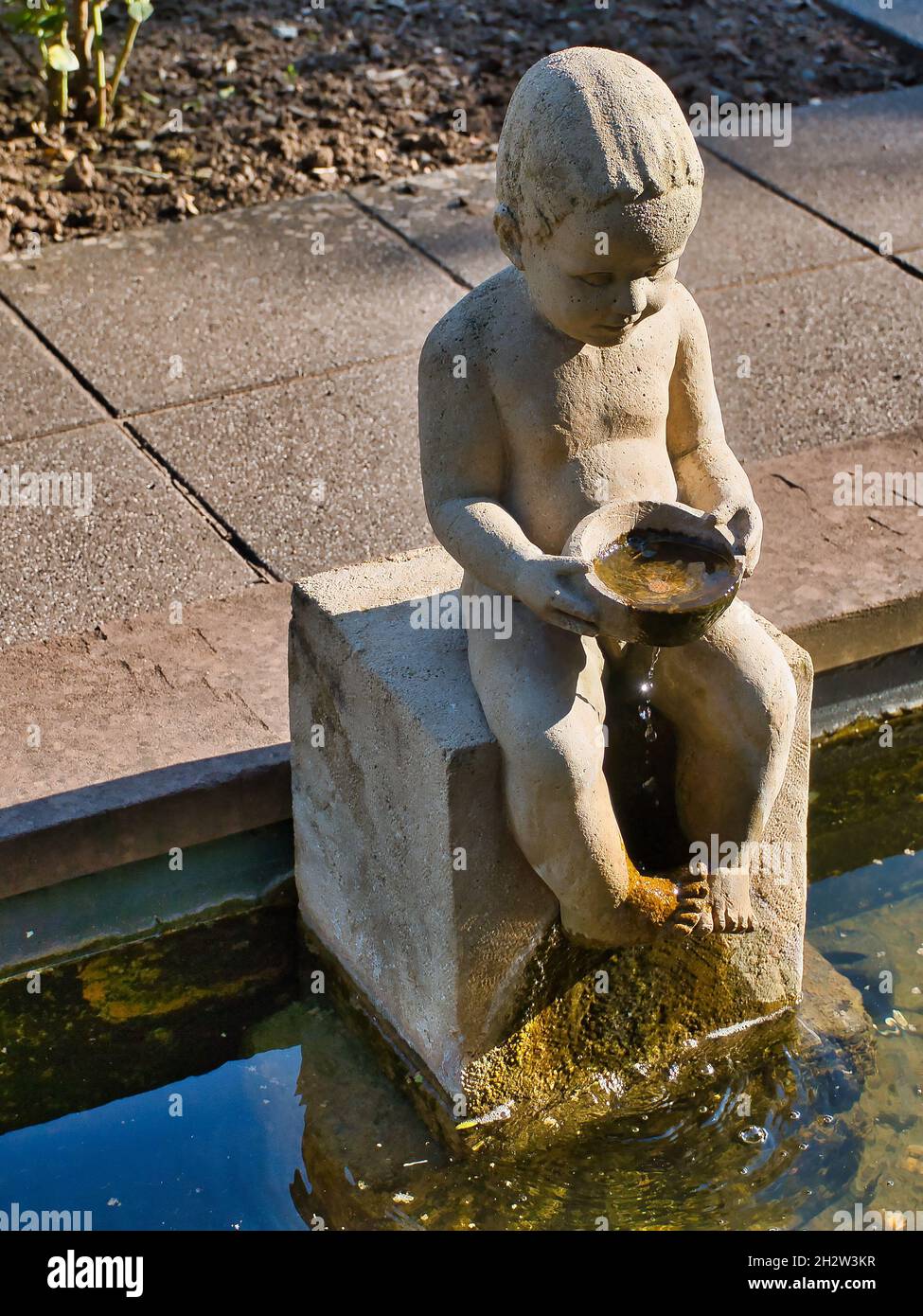 A statue of a little boy sitting on a stone Stock Photo - Alamy
