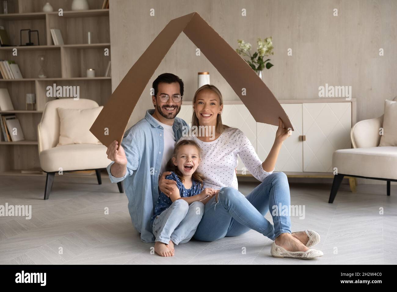 Portrait of smiling beautiful young family sitting under carton roof ...