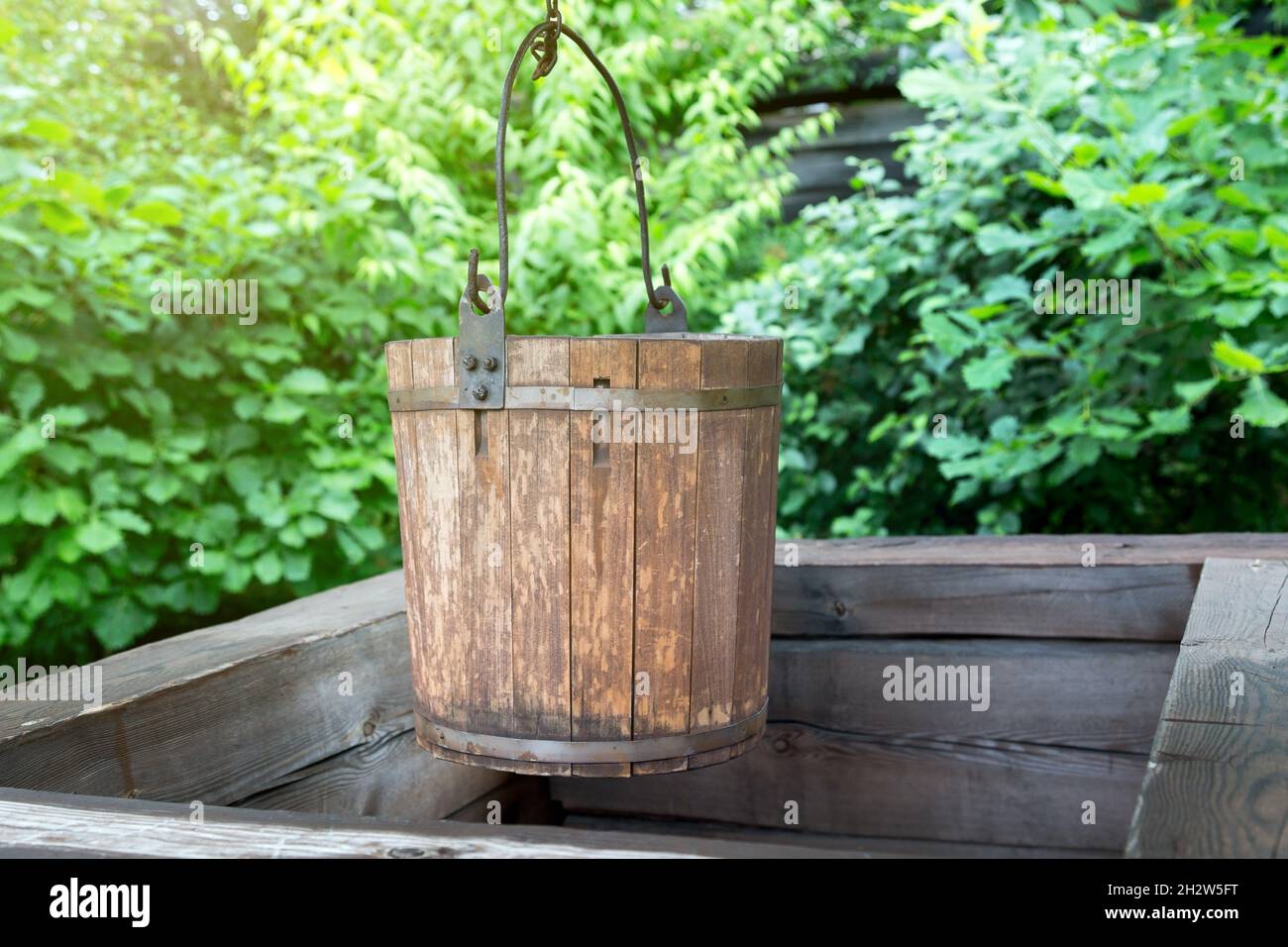 Wooden well with a bucket on a chain on background of green trees Stock ...