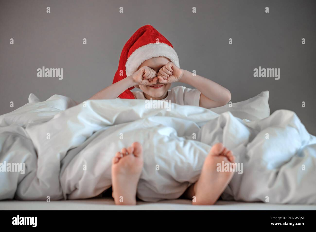 Funny cute boy waking up and rubing your eyes in a Santa hat. Happy ...
