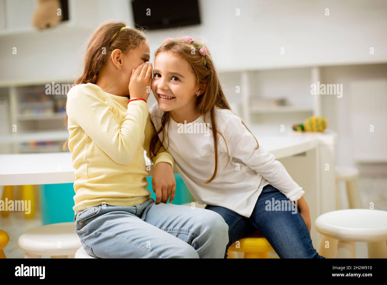 Cute little girl whispering something in an ear of her friend Stock ...