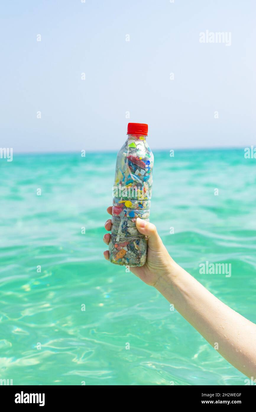 A person holding a plastic bottle filled with microplastics against the ...