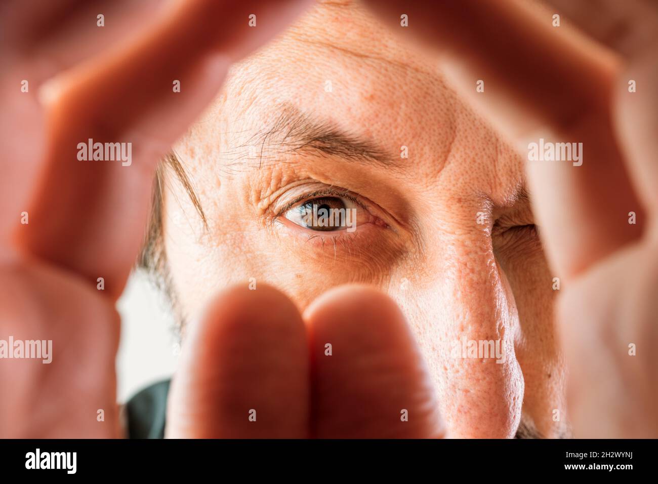 Man peeking through cupped hands, selective focus Stock Photo - Alamy