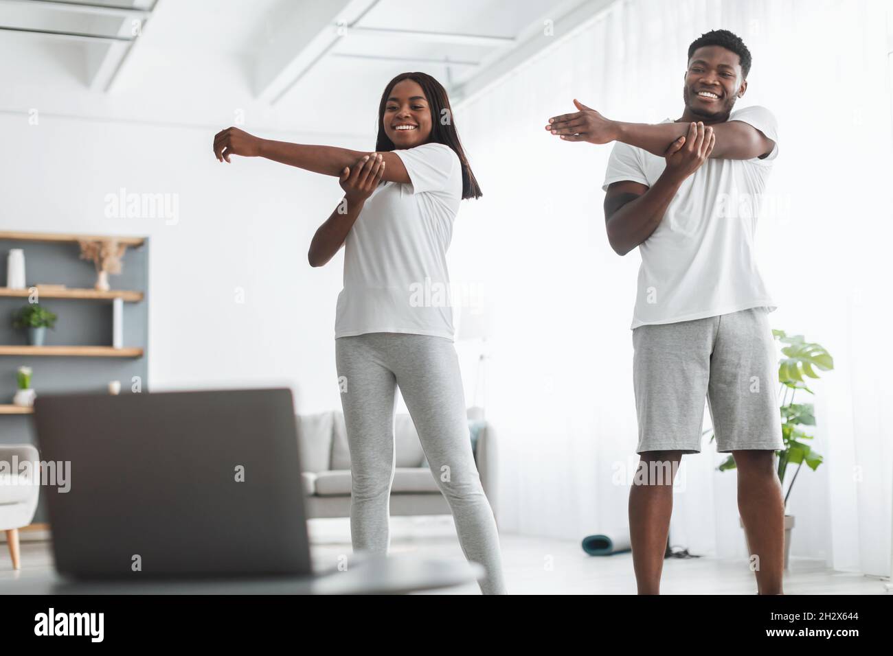 Young black couple doing arm stretch exercise watching online tutorial ...
