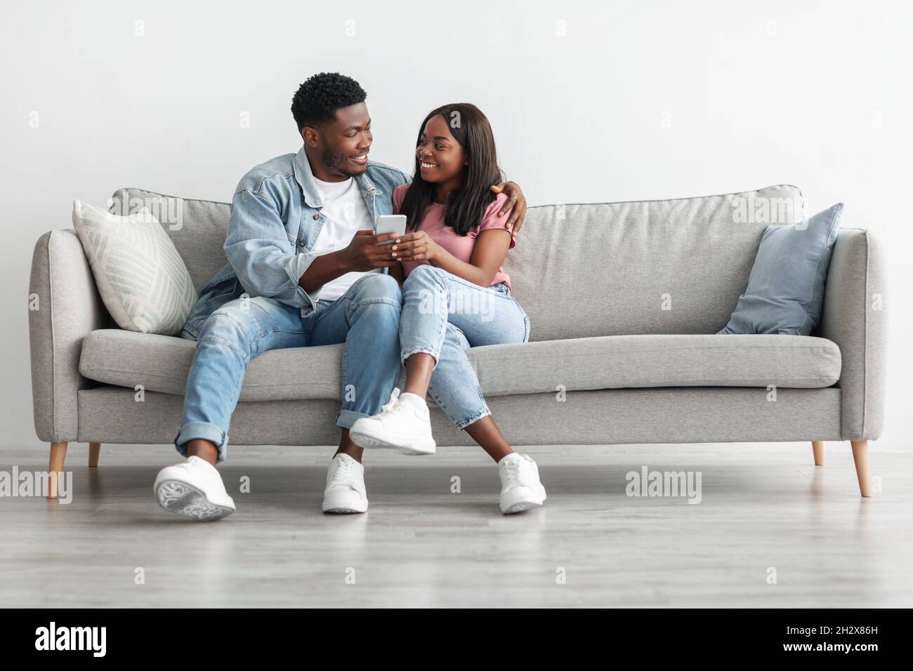 Happy black couple sitting on couch, sharing using cellphone Stock ...