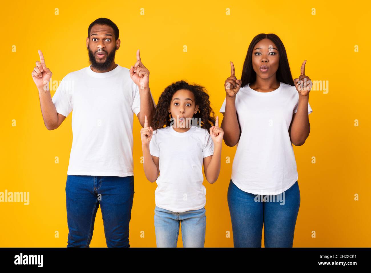 Surprised black family pointing up at free space at studio Stock Photo ...