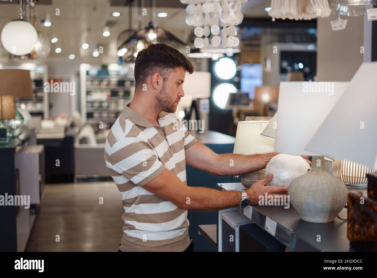 Side view of man in casual clothes inspecting stylish modern lamp while ...