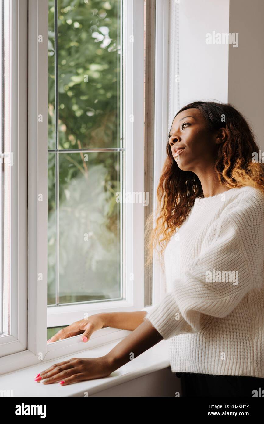 A beautiful young black elegant female leaning on the windowsill ...
