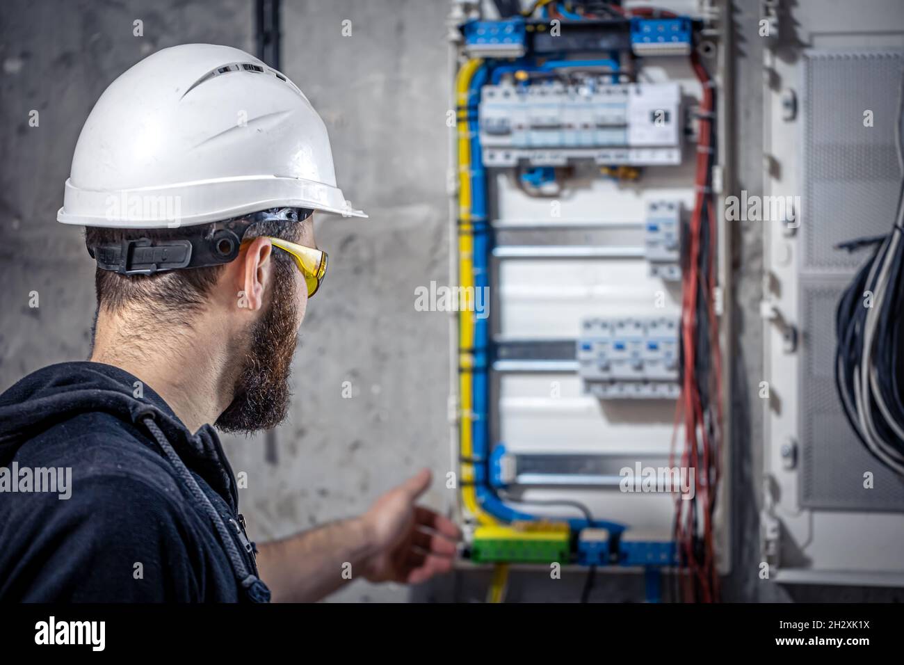 A male electrician works in a switchboard with an electrical connecting ...
