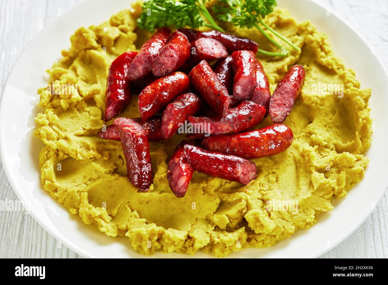 mashed green peas with fried deviled sausages on white plate on a white ...