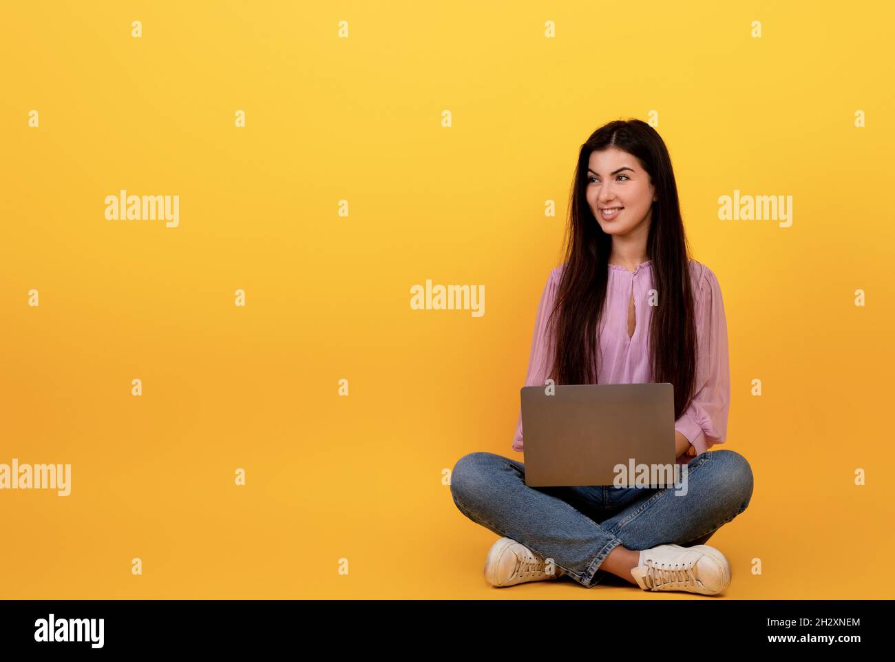 Happy armenian woman using laptop computer on yellow studio background ...