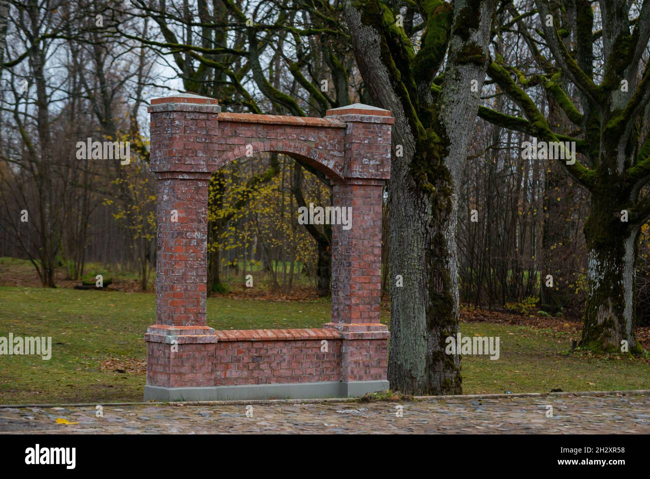Red brick arch in the park with oak trees overgrown with green moss on ...