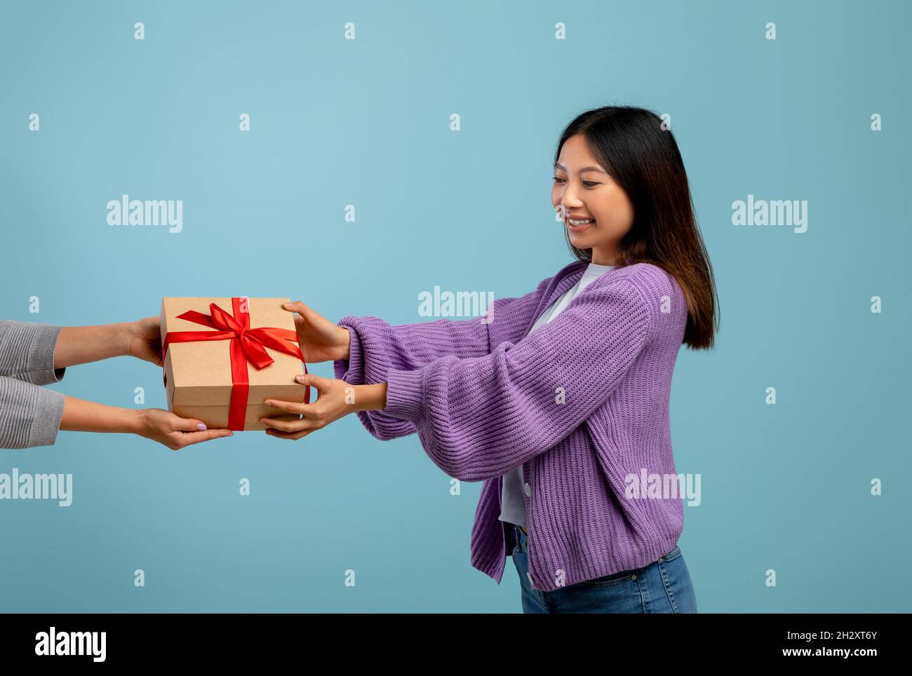 Happy asian lady receiving wrapped gift box, standing over blue studio ...