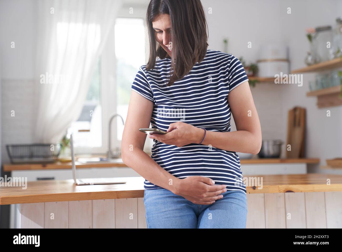A young pregnant woman with a smile holds her stomach with one hand ...
