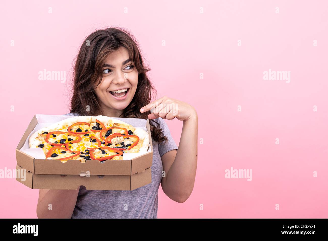 Attractive girl with pizza in a box for delivery on a pink background ...