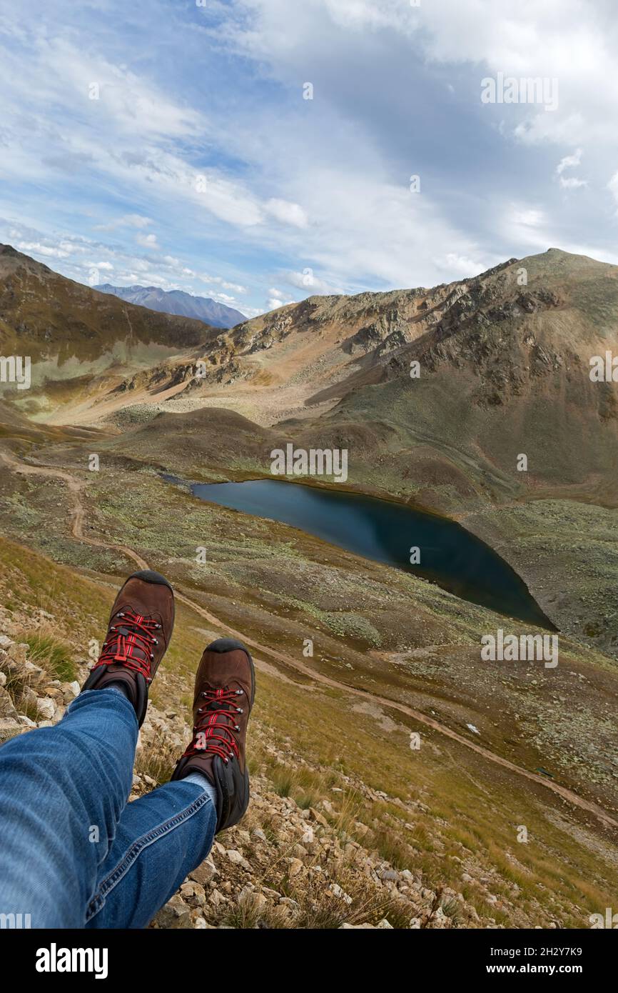 Feet of a tourist in trekking boots on a high hill above a mountain ...