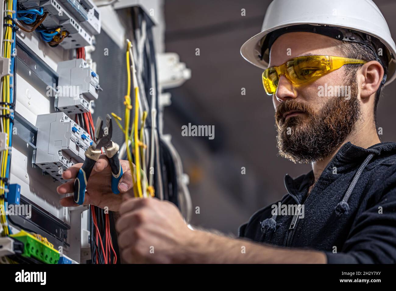 A male electrician works in a switchboard with an electrical connecting ...