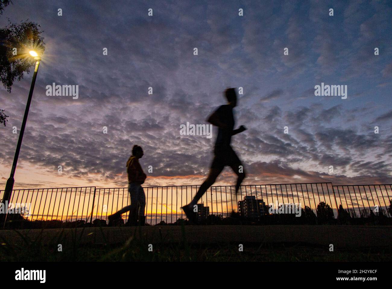 Running as the sun sets in an urban park in London with a tower block ...
