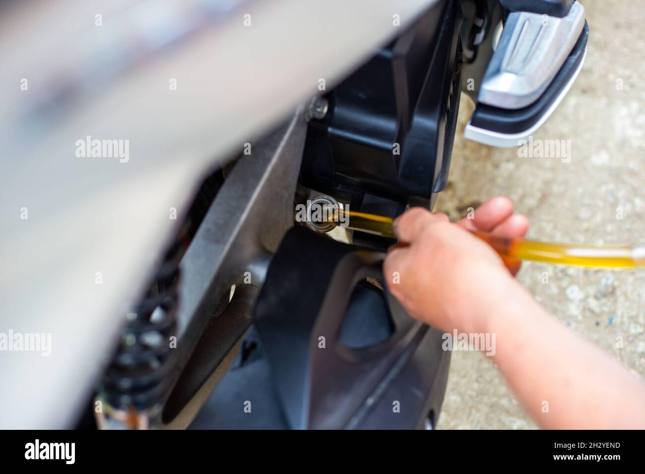 A car mechanic pours engine oil through a tube into a motorbike engine ...