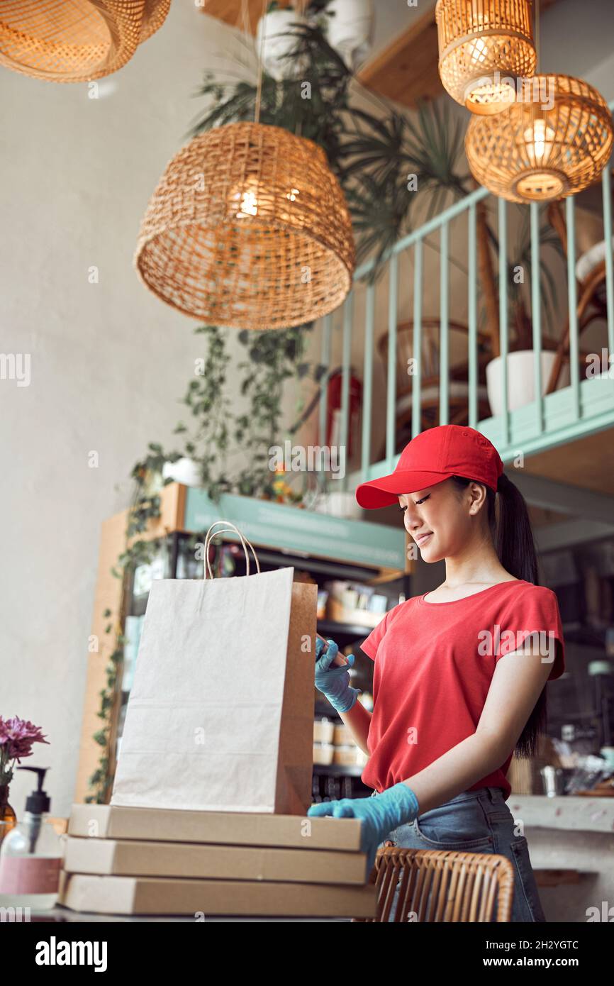 Female delivery worker packing food orders indoors Stock Photo - Alamy