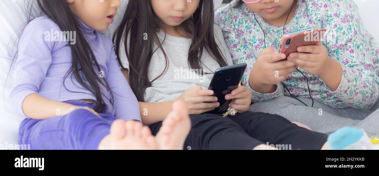 Happy asian little kid and friends playing smartphone on sofa at home ...