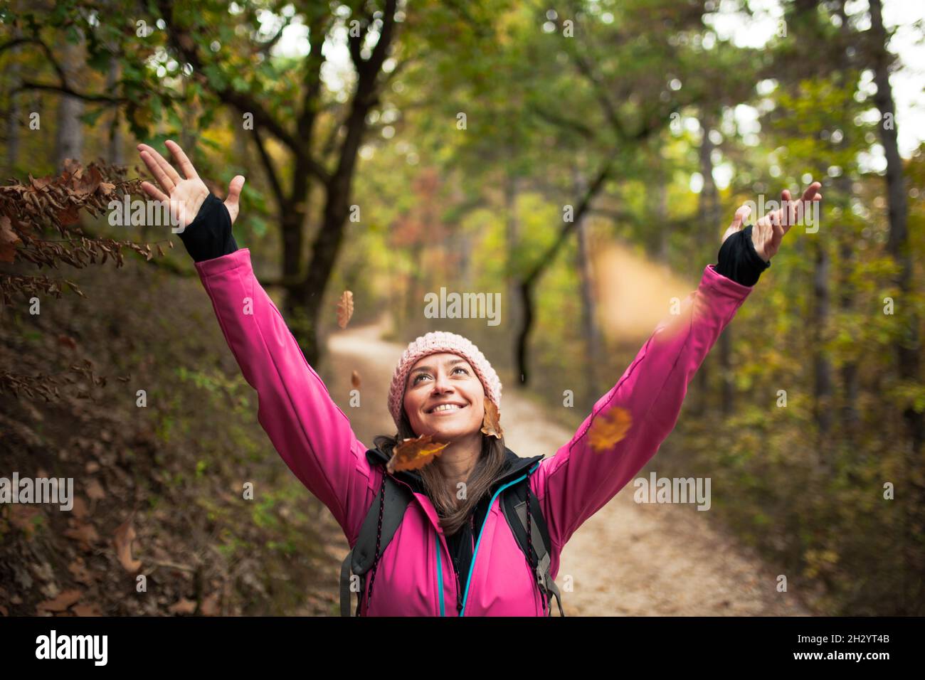 Hiking girl in pink on a trail in the forest. Hands up enjoying the ...