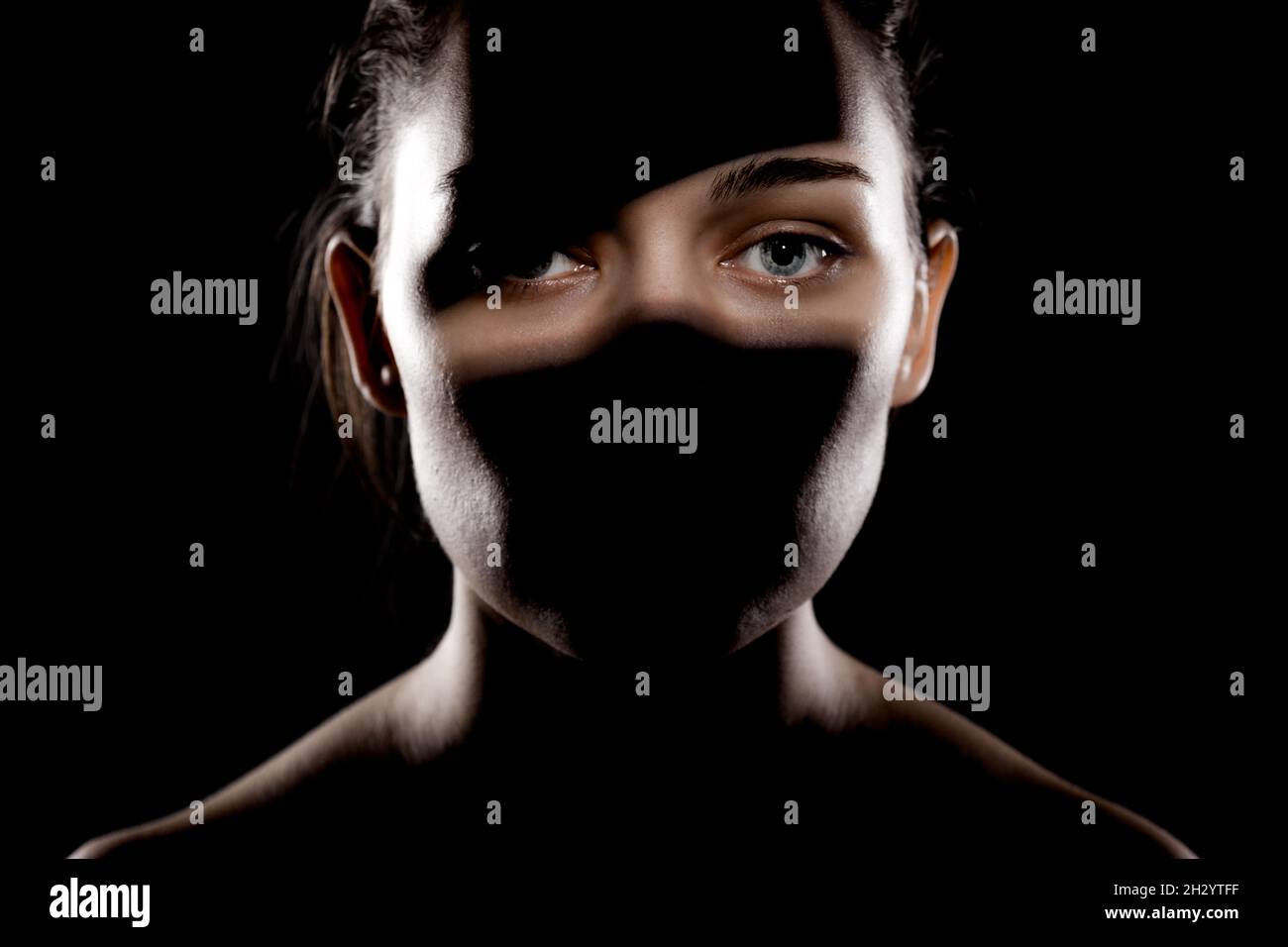 studio portrait of a beautiful young woman with shadows on her face ...