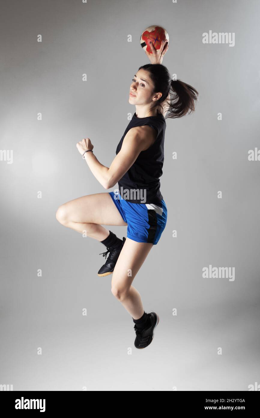 Handball player posing on light gray background. Girl jumping with ball ...