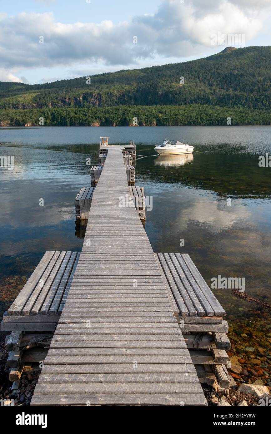 A long wooden boat wharf with a white boat moored. The plank pier juts ...