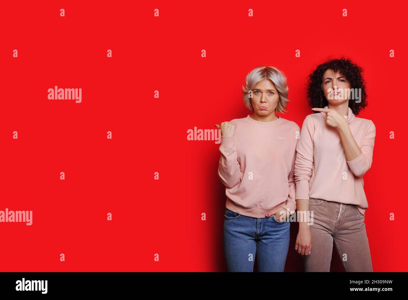 Portrait of two sad young women standing together and looking at camera ...