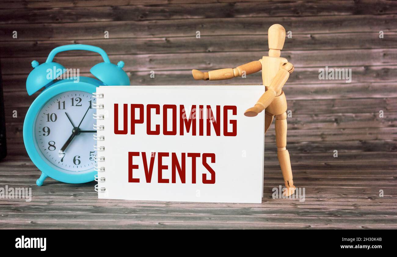 Upcoming event message on notepad with wooden doll and alarm clock on ...
