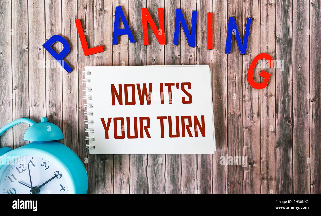 words NOW ITS YOUR TURN written on a notepad and a wooden table ...