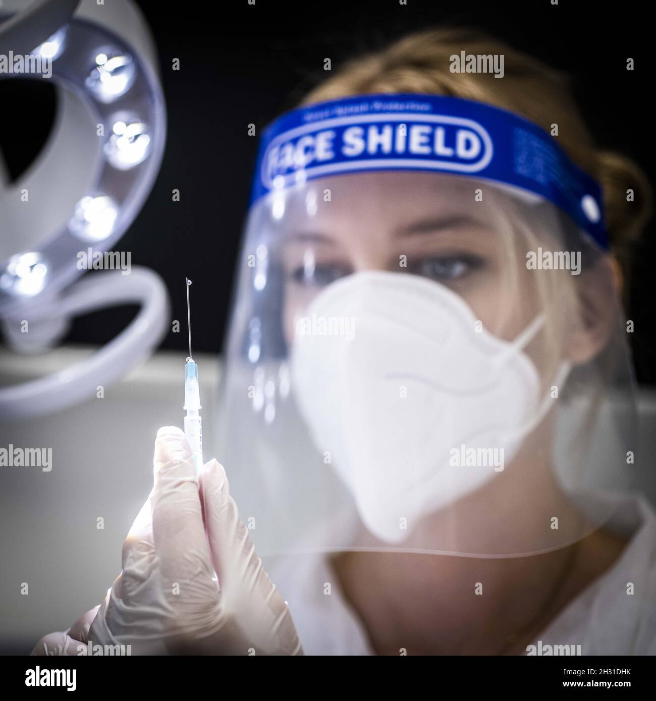 A nurse wearing full ppe, face mask and shield prepares a syringe for ...