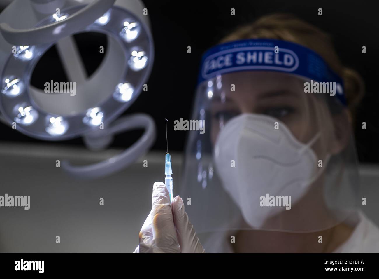 A nurse wearing full ppe, face mask and shield prepares a syringe for ...