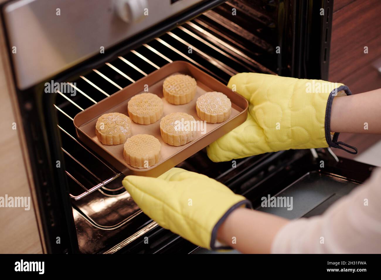 Woman in baking gloves putting tray with mooncakes in preheated oven ...