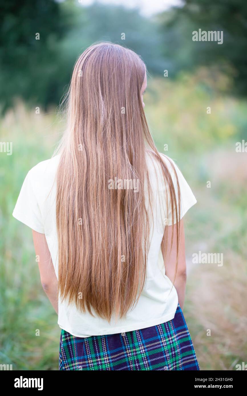 A girl with long white hair from behind against a background of a green ...