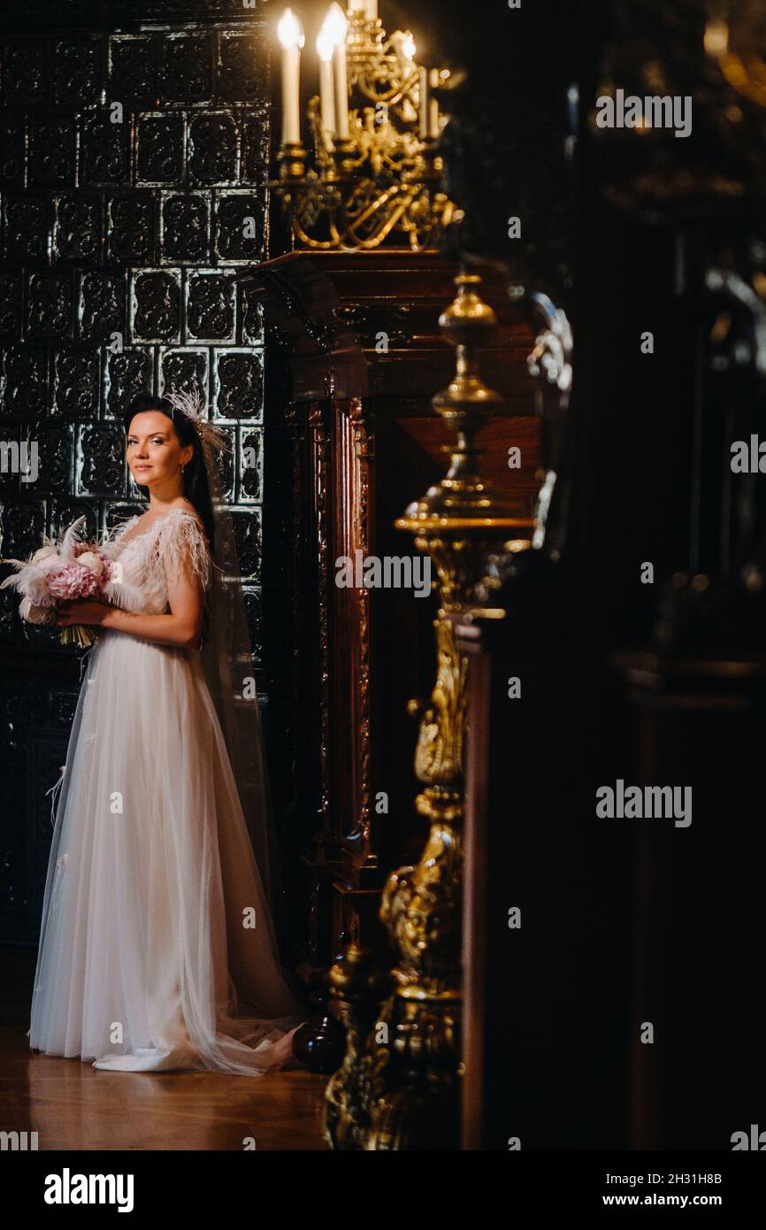 The bride in a wedding dress and with a bouquet stands at the old ...