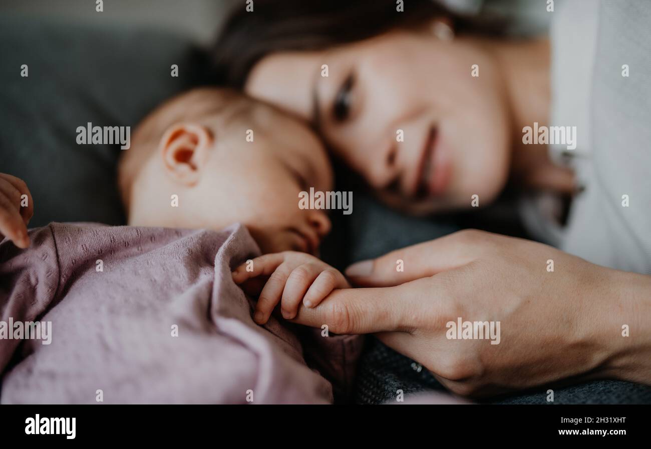 Happy young mother touching her newborn baby girl, lying on sofa ...