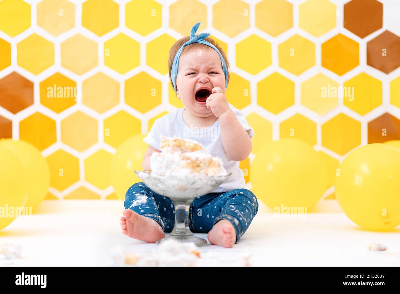Birthday. A crying dirty baby girl is sitting next to a broken cake. In ...