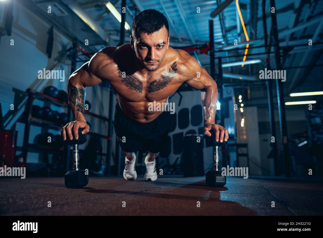 Fronr view of muscled athlete, bodybuilder workouts alone at sport gym ...